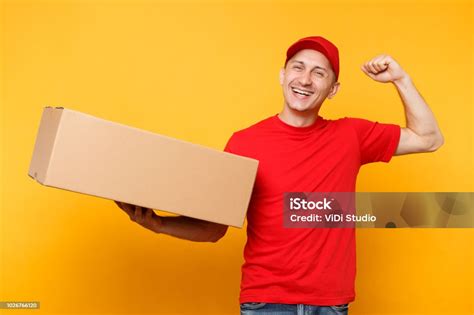 빨간색 유니폼 노란색 오렌지 배경에 고립 된 배달 남자 전문 남성 직원 택배 또는 대리점에 빈 골 판지 상자를 들고 T셔츠 모자 수신 패키지 서비스 개념입니다 공간 복사