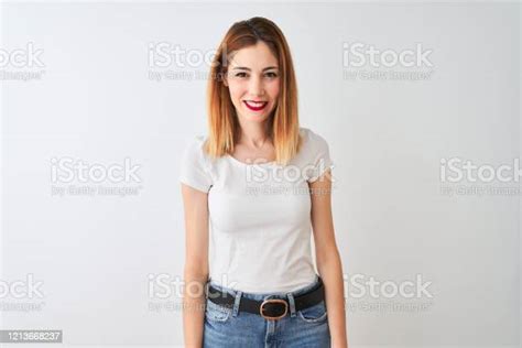 편안한 흰색 배경 위에 서있는 캐주얼 한 빨간 머리 여성은 얼굴에 미소를 지으며 옆으로 바라보고 자연스러운 표정 자신감 있게 웃고 있습니다 T 셔츠에 대한 스톡 사진 및