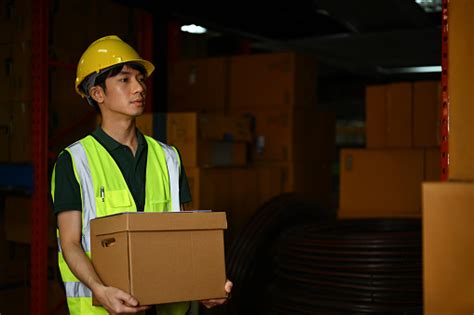 안전모와 조끼를 입은 아시아 남성 노동자가 골판지 상자를 들고 대형 소매 창고를 걷고 있다 25 29세에 대한 스톡 사진 및 기타 이미지 25 29세 Group A