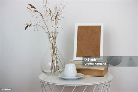 마른 풀이 있는 유리 꽃병 접시가 달린 하얀 커피 한 잔 하얀 프레임이 하얀 벽에 하얀 침대 옆 탁자 위에 오래된 책 위에 서 있다 0명에 대한 스톡 사진 및 기타 이미지