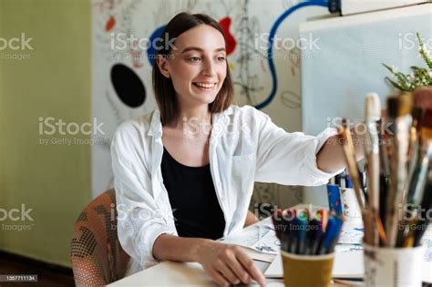 책상속의 젊은 화가가 집에서 배경에 큰 패턴 캔버스가 있는 페인트 브러시를 즐겁게 선택합니다 25 29세에 대한 스톡 사진 및 기타 이미지 Istock