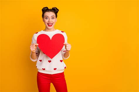 예쁜 애정 레이디 홀드 페이퍼 하트 쇼 예기치 않은 날짜 엽서 부드러운 감정을 입고 흰색 빨간 하트 패턴 스웨터 바지 고립 된 노란색 배경 갈색 머리에 대한 스톡 사진 및