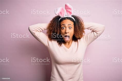 젊은 아프리카 계 미국인 여자 와 Afro 머리 입고 토끼 귀 위에 분홍색 배경 미친 과 무서워 손에 머리에 두려워 하 고 충격의 놀란 와 오픈 입 감정에 대한 스톡 사진