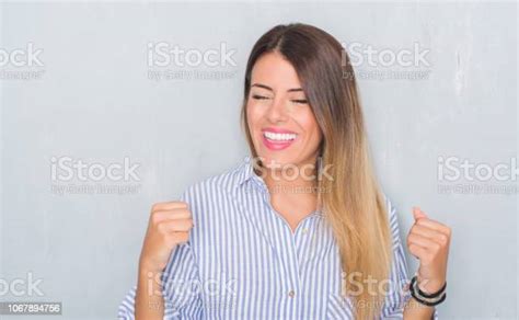 그런 지 위에 젊은 성인 여자 회색 벽 매우 행복 하 고 흥분 무기와 우승자 제스처를 하 고 비즈니스 셔츠를 입고 웃 고 성공을 위한 비명 축 하 개념입니다 갈색 머리에