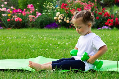 흰색 티셔츠를 입은 어린 귀여운 소녀 13은 꽃의 배경에 녹색 매트에 아령과 스포츠에 간다 T 셔츠에 대한 스톡 사진 및 기타