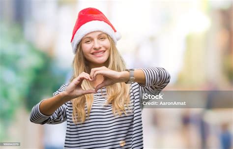 젊은 아름 다운 금발 여자 마음 기호와 손으로 모양을 보여주는 사랑에 웃 고 고립 된 배경 위에 크리스마스 모자를 쓰고 낭만적인 개념입니다 개념에 대한 스톡 사진 및 기타