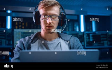 Portrait Of Software Developer Hacker Gamer Wearing Glasses And Headset Sitting At His Desk And