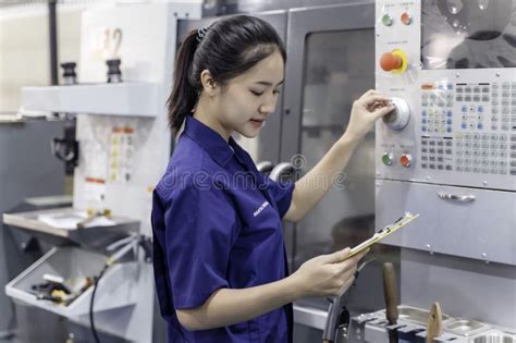 Asian Woman Industrial Engineer Wearing Uniform Looking At A Clipboard And Checking Automated