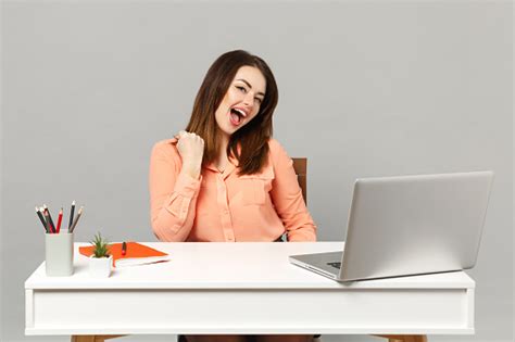 파스텔 옷에 젊은 즐거운 여자는 예 앉아 회색 배경에 고립 된 Pc 노트북과 책상에서 작업을 말하고 위 너 제스처를 하 고 있습니다 성취 비즈니스 커리어 라이프 스타일 컨셉