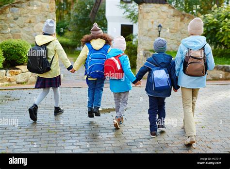Rear View Of Classmates Holding By Hands And Moving To School Stock