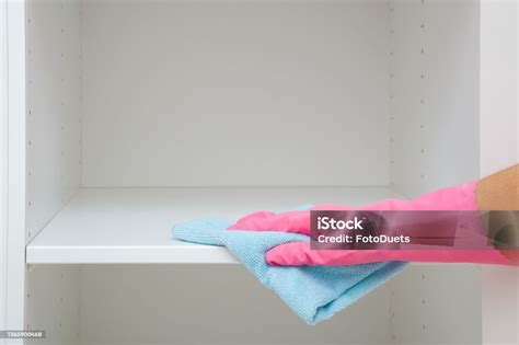 젊은 성인 여성은 파란색 드라이 걸레를 사용하여 분홍색 고무 보호 장갑을 착용하고 방에있는 나무 옷장 안에 흰색 선반을 닦아 손에 근접 촬영 전면 보기입니다 집에서 정기적
