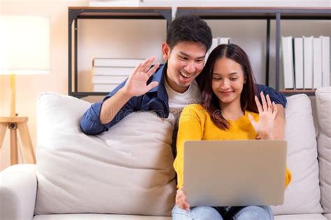 Happy Asian Couple Video Call On Laptop Sitting On Sofa In Living Room