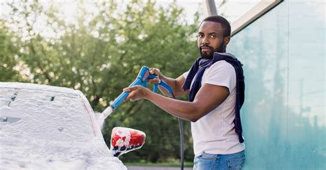 고압 제트를 사용하여 비누 거품으로 자동차의 실외 청소 잘 생긴 수염을 기른 아프리카 청년이 야외에서 셀프 세척 서비스에서