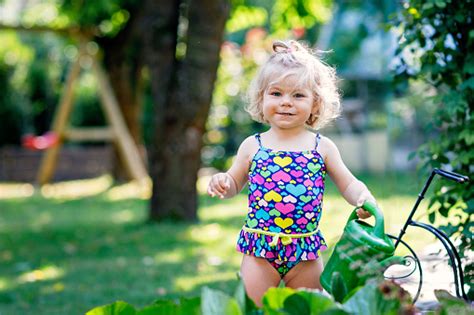 화려한 수영복을 입은 귀여운 어린 소녀는 더운 여름날 국내 정원에서 식물과 꽃이 만발한 식물에 물을 줍니다 물과 Ca를 가지고 노는 재미를 가진 사랑스러운 유아 아이 감정에