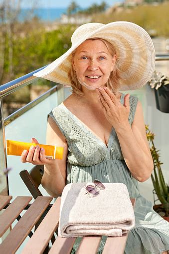 바닷가에 있는 호텔 테라스에 있는 여성 무두질 어깨에 선 크림을 적용 하는 여자 자외선 차단 스킨 및 바디 케어 바다에 대한