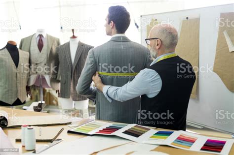 후면 보기의 대머리 수염 재 스튜디오에서 피팅 하는 동안 다시 테이프 측정으로 Businessmens의 크기를 측정 하는 검은 조끼에 수석 재단사 2명에 대한 스톡 사진 및