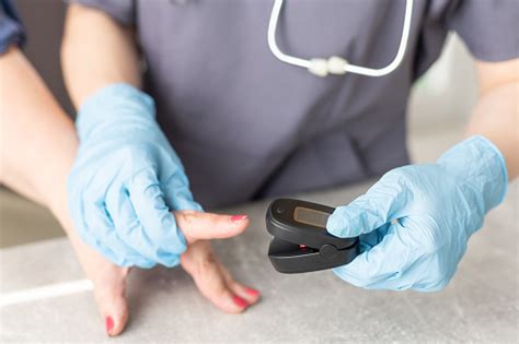 집에서 의료 지원 의료 용 마스크의 여성 의사는 소파에 앉아있는 동안 맥박 산소계를 사용하여 중년 여성에게 환자의 맥박과 산소 포화를 측정합니다 2명에 대한 스톡 사진 및