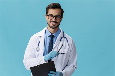 흰 코트와 안경을 쓴 남자 의사 의료 기록과 청진기가 있는 파란색 고립된 배경 복사 공간 텍스트 공간에 미소를 짓고 있습니다 25 29세에 대한 스톡 사진 및 기타 이미지