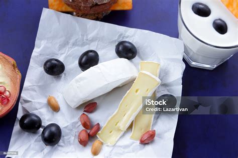 카망베르 치즈 오렌지 대리석 치즈 우유 석류 올리브 땅콩 알갱이 어두운 파란색 포도 흰색 직물 및 진한 파란색 배경 복고 스타일 치즈 배경 빵의 유리 0명에 대한 스톡 사진