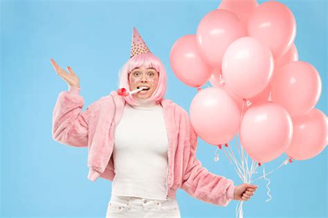 모피 코트를 입은 어린 휴가 소녀 분홍색 풍선을 들고 입에 휘파람과 생일 모자를 착용 당황과 놀라움 파란색 배경에 고립 20 29세에 대한 스톡 사진 및 기타 이미지