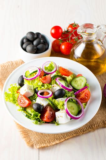 체리 토마토 Ruccola Arugula 죽은 태아 올리브 오이 양파 향신료로 만든 신선한 그리스 샐러드 나무 배경에 흰색 그릇에 시저 샐러드 건강 한 유기농 다이어트 식품