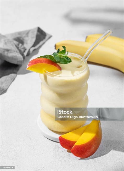 망고와 바나나를 곁들인 냉동 스무디는 열대 과일 조각과 그림자가 있는 밝은 배경에 유리잔에 담겨 있습니다 망고에 대한 스톡 사진 및 기타 이미지 Istock