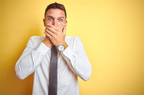 노란색 고립 된 배경 위에 우아한 흰색 셔츠를 입고 젊은 잘 생긴 사업가 실수로 손으로 입을 덮는 충격 비밀 개념입니다 가리기에