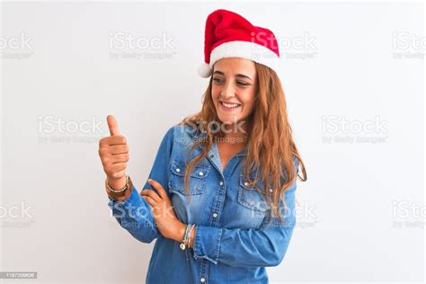 고립 된 배경을 통해 크리스마스 모자를 입고 젊은 아름다운 빨간 머리 여자 자랑찾고 옆으로 엄지 손가락을하고 미소 긍정적인 감정 표현에 대한 스톡 사진 및 기타 이미지