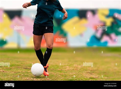 View of legs of brunette female soccer player running to kick soccer ball. on a green grass ...