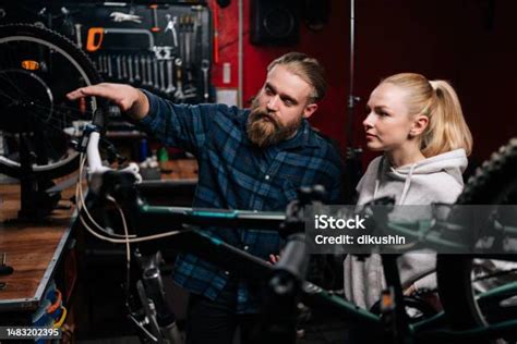 금발의 여성 고객과 의사 소통하는 수염 난 자전거 수리공의 정면보기 수리점에서 진단 중에 감지 된 자전거의 문제에 대해 이야기 자동차 수리 공장에 대한 스톡 사진 및 기타