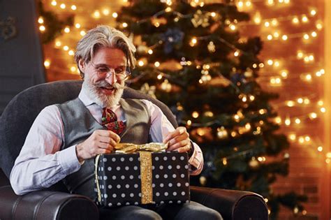 ภาพของผู้สูงอายุที่มีสไตล์ที่มีผมสีเทาและเคราอยู่ในห้องคริสต์มาสตกแต่งด้วยกล่องของขวั ภาพสต็อก