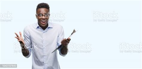 젊은 아프리카계 미국인 남자는 Clipboarad 매우 행복 하 고 흥분 상자 식 큰 웃음 소리는 승리를 축 하 하 고 손을 들고 검사 보기에 대한 스톡 사진 및 기타