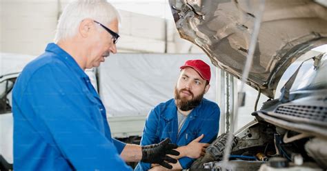 기술 서비스의 젊은 수염 난 노동자는 그의 말을 들으면서 대형 기계의 고장난 엔진을 검사하는 성숙한 동료를 바라보고 있습니다 사진 Unsplash의 자동차 이미지