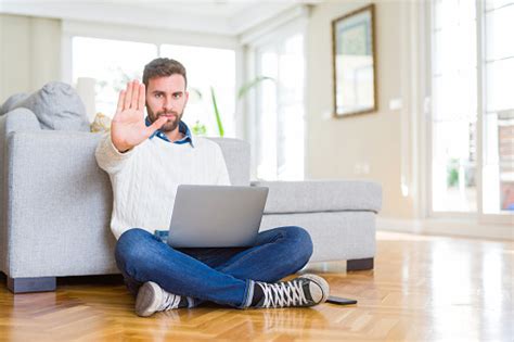 진지하고 자신감있는 표정 방어 제스처로 정지 표지판을하고 열린 손으로 컴퓨터 노트북을 사용하여 작업하는 잘 생긴 남자 가정