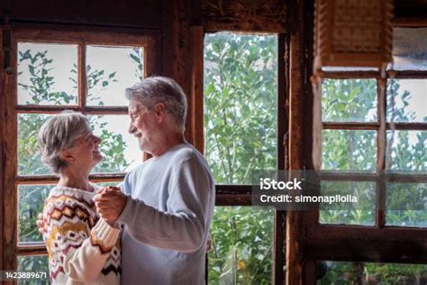 노인과 여자 행복한 커플은 야외 배경과 창문이있는 거실에서 집에서 춤을 추고 있습니다 노인들은 겨울 방학을 위해 샬레를 함께