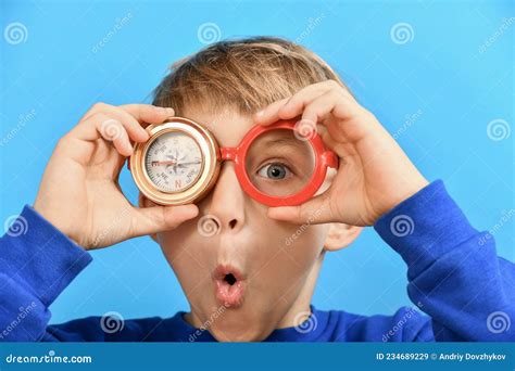 A Funny And Surprised Boy Holds A Compass In One Hand Near His Eyes And