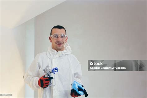 공기없는 스프레이 페인트 작업자는 흰색으로 공기가 없는 스프레이로 벽을 페인트하고 숙련된 작업자가 기계식 공기 도구로 표면에 페인트를 분사합니다 전문 기술에 대한 스톡 사진