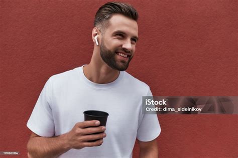 젊고 행복합니다 잘 생긴 수염 남자 에 헤드폰 들고 컵 커피와 미소 동안 빨간 벽에 대 한 야외 가까이 옴에 대한 스톡 사진 및 기타 이미지 Istock