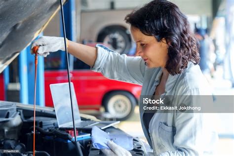 자동차 정비소에 서서 장갑과 캐주얼 한 옷을 입고 수동 자동차 유지 보수 기술 및 전문 지식을 착용하면서 자동차 엔진의 오일 계량봉을 집중적으로 점검하는 여성 정비사 35