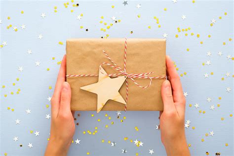 줄무늬 빨간 리본과 황금 색종이 별 파스텔 블루 배경 위에 나무 별 선물 상자를 들고 여성의 손 크리스마스 새해 겨울 휴일 및 생일 개념입니다 2020년에 대한 스톡 사진