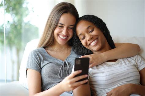 Casal Lésbica Interracial Feliz Checando O Celular Em Um Sofá Foto de Stock Imagem de feliz