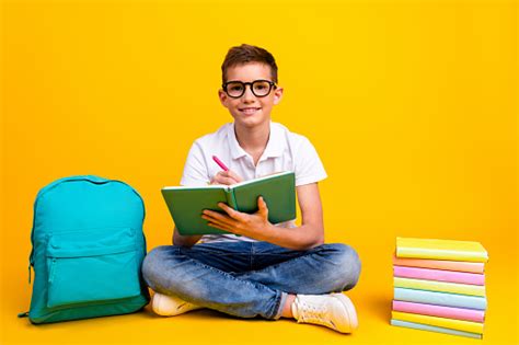 쾌활한 긍정적 인 소년 옷을 입은 폴로 티셔츠 배낭 쓰기 책 Emtpy 공간 외딴 노란색 배경의 전체 길이 사진 12 13세에