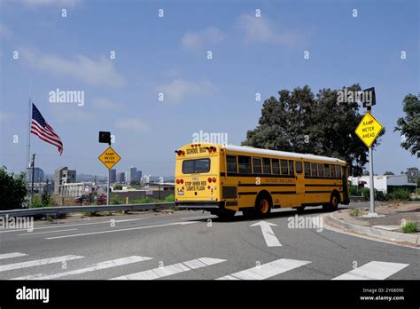 A Yellow School Bus Navigates An Urban Road Near A City Skyline With