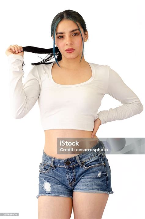 염색 한 푸른 머리와 포니 테일을 한 아름 다운 젊은 여성의 초상화 긴 소매 크롭 탑과 짧은 청바지를 입고 흰색 배경에 등 뒤로 손을 대고 있습니다 18 19세에 대한 스톡