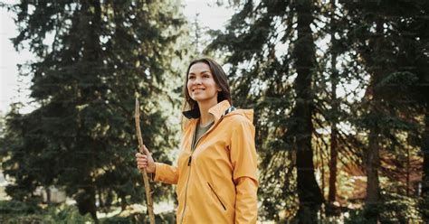 용감한 등산객 노란 재킷을 입은 귀여운 소녀의 초상화는 손에 나뭇가지가 있고 햇볕이 잘 드는 침엽수 림에서 시간을 보내고 있다 그녀는 미소로 시선을 돌리고 있다 사진