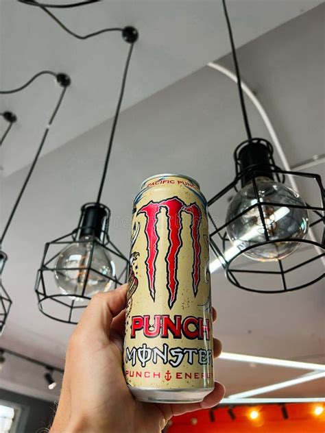 Hand Holding A Monster Punch Energy Drink Can Against A Modern Lamp