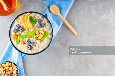 회색 배경에 블루 베리 견과류와 꿀오트밀 그릇 사과와 신선한 민트가 달린 오트밀 죽이 블루 냅킨에 새겨서 공간을 복사합니다 위쪽 보기 0명에 대한 스톡 사진 및 기타 이미지