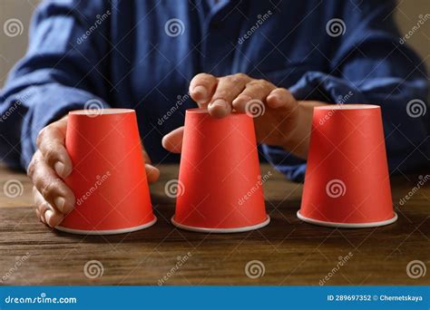 Woman Playing Thimblerig Game With Red Cups At Wooden Table Closeup