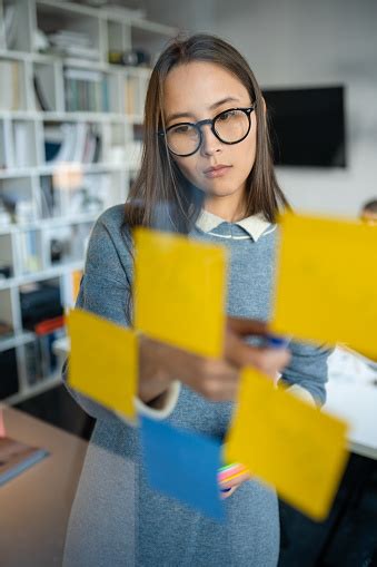 젊은 비즈니스 우먼 브레인 스토밍 아시아 여자 유리 벽에 부착 된 스티커 노트에 아이디어를 작성합니다 비즈니스 성공 개념 개발에