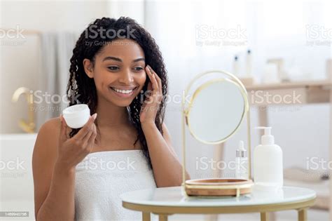 매력적인 젊은 아프리카계 미국인 여성이 얼굴에 보습 크림을 바르고 있다 25 29세에 대한 스톡 사진 및 기타 이미지 25 29세 가꿔주기 가정 생활 Istock